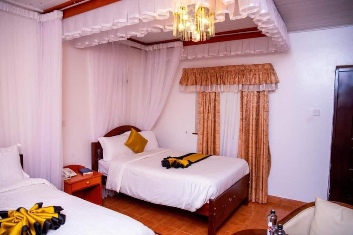 Quarto de hotel com duas camas, cabeceira de madeira, mesa de cabeceira com telefone e um candelabro.