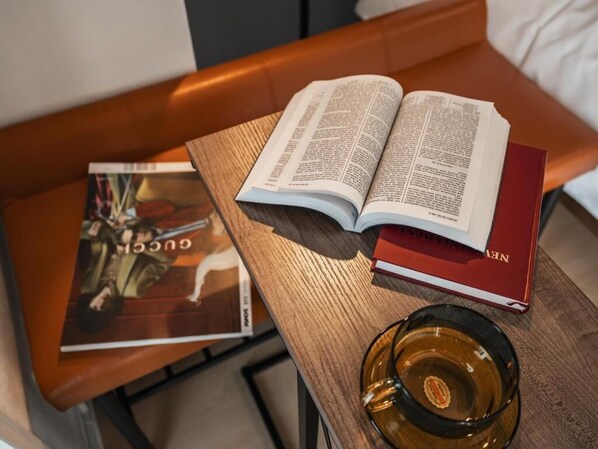 Um livro aberto sobre uma mesa de madeira, um livro fechado ao lado, e uma caneca de vidro com um saquinho de chá.