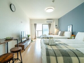 Quarto de hotel com cama, escrivaninha, cadeira, mesinha de apoio e janela com cortinas.