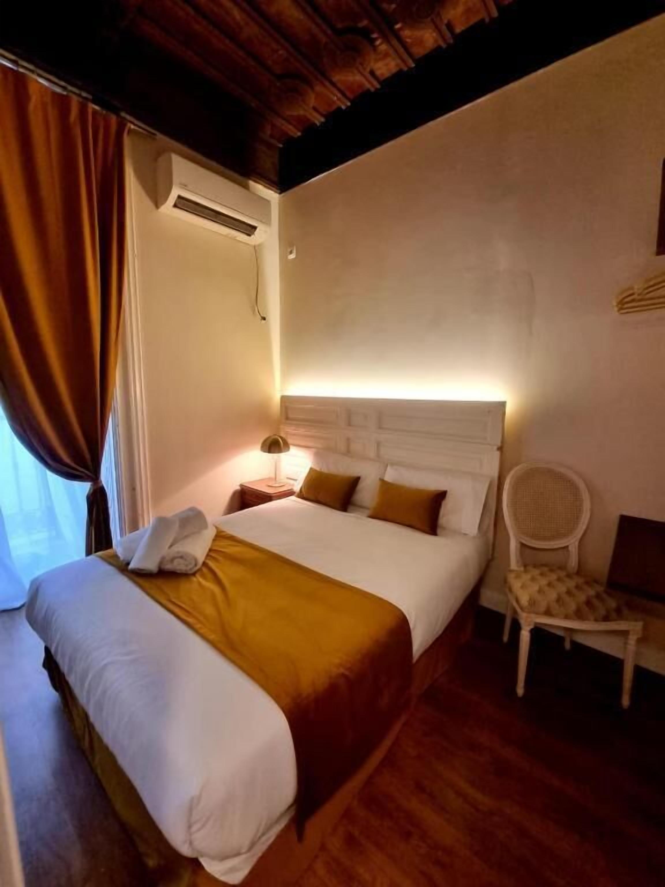 Quarto de hotel com uma cama, uma cadeira, uma mesinha de cabeceira e um aparelho de ar condicionado.