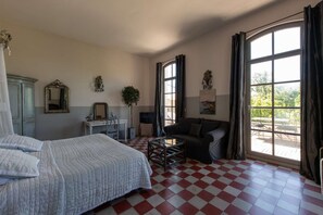 Quarto com cama, escrivaninha, cadeira, sofá e janelas amplas.