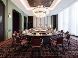 Uma sala de conferências com uma mesa redonda, cadeiras vermelhas e um candelabro.