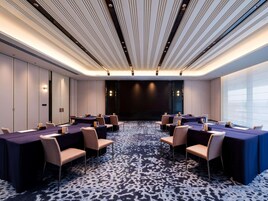 Sala de conferências com carpete estampado, várias mesas com cadeiras e design de teto moderno.