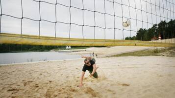 Uma rede de voleibol com quadra de areia e um corpo d'água ao fundo.