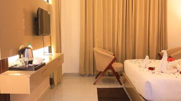 Quarto de hotel com cama, escrivaninha, cadeira, televisão e cortina.
