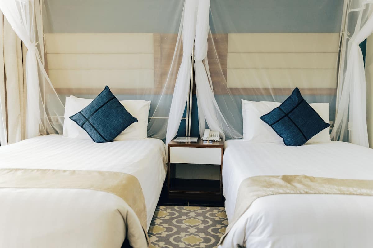 Quarto de hotel com duas camas, uma mesa de cabeceira com telefone e uma cama com dossel.