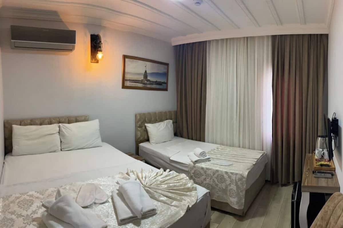 Quarto de hotel com duas camas, uma escrivaninha com abajur e um quadro na parede.