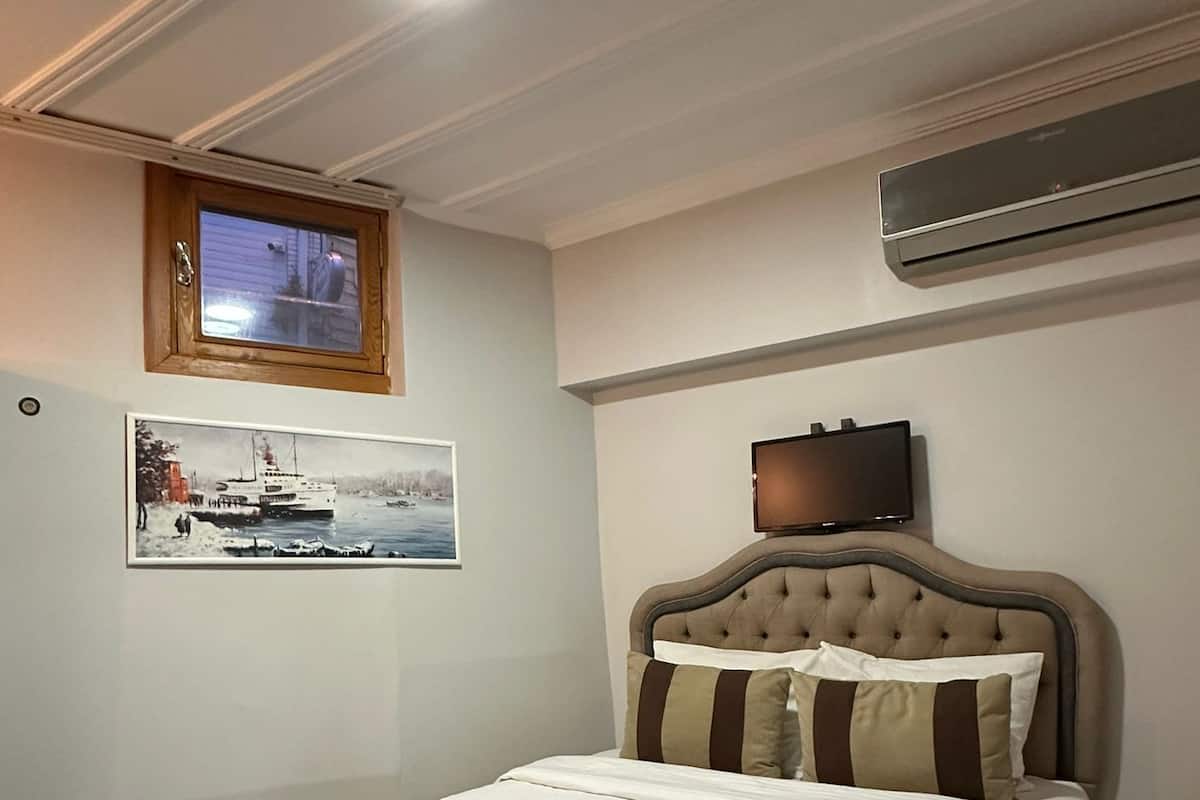 Quarto com cama, TV montada, janela com vista e ar condicionado.