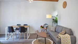 Uma sala de estar moderna com área de jantar, apresentando teto de madeira, tapete redondo, sofá cinza, poltrona colorida e mesa de jantar com cadeiras.