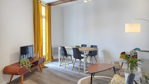 Uma sala de estar moderna com mesa de jantar de madeira, cadeiras pretas, televisão e sofá.