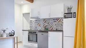 Cozinha compacta com armários brancos, micro-ondas, lava-louças e painel de azulejos.