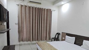 Quarto de hotel com cama, uma cadeira, televisão e cortina.