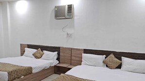 Quarto de hotel com duas camas, cabeceira de madeira, ar condicionado fixado na parede e uma pequena mesa de cabeceira.