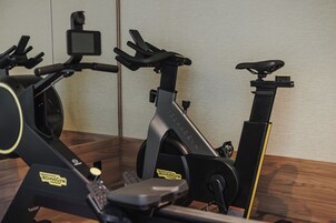 Três bicicletas ergométricas estacionárias com painéis de controle, uma delas com um dispositivo montado no guidão.