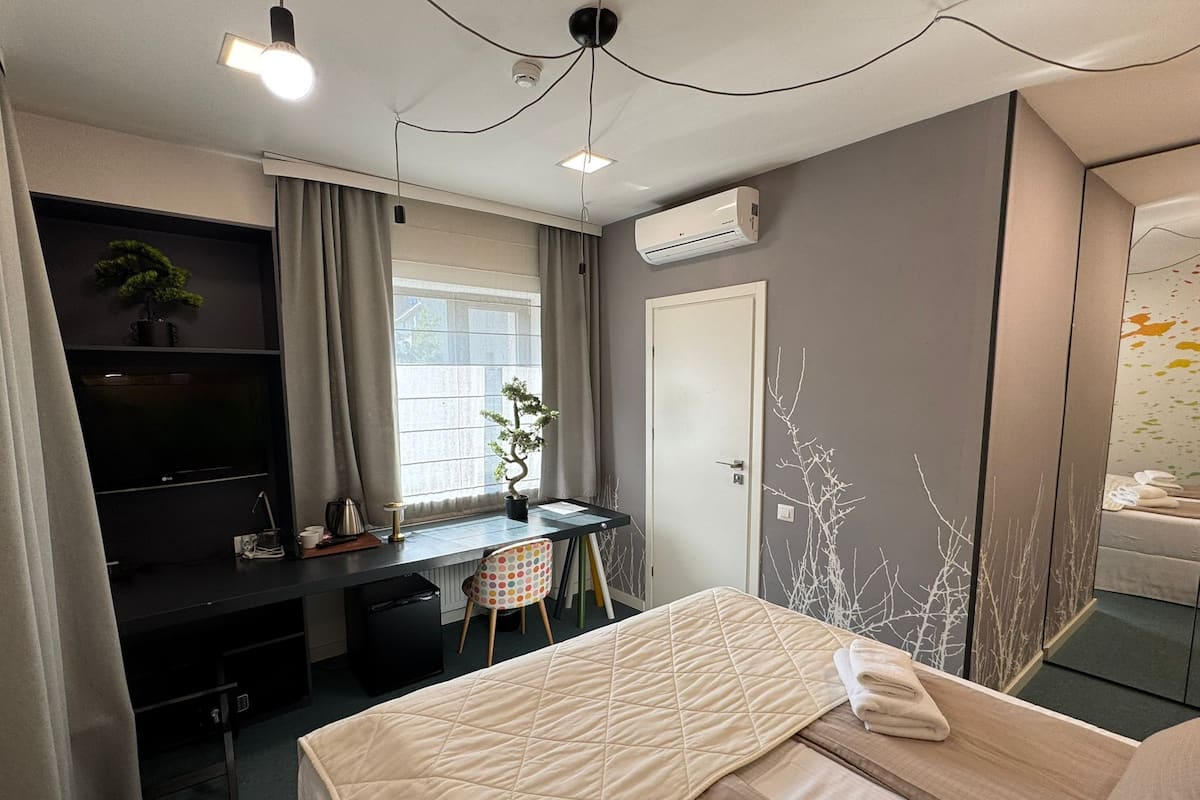 Quarto moderno com cama, escrivaninha, televisão e ar condicionado.