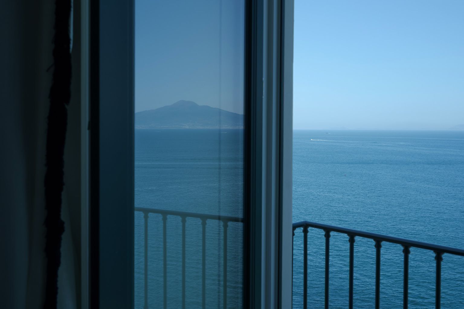 Vista de uma varanda com guarda-corpo, com vista para um corpo d'água e uma montanha distante.