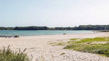Uma praia com areal, um cais e águas calmas.