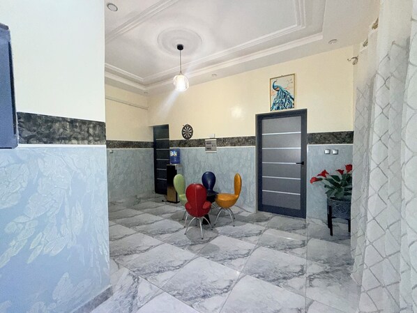 Um corredor com piso ladrilhado, teto com luminária, uma porta e uma parede com um quadro emoldurado.