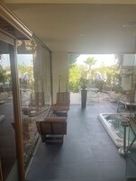 Uma área de spa com bancos de madeira, uma banheira de hidromassagem e uma parede de vidro com vista para o jardim externo.