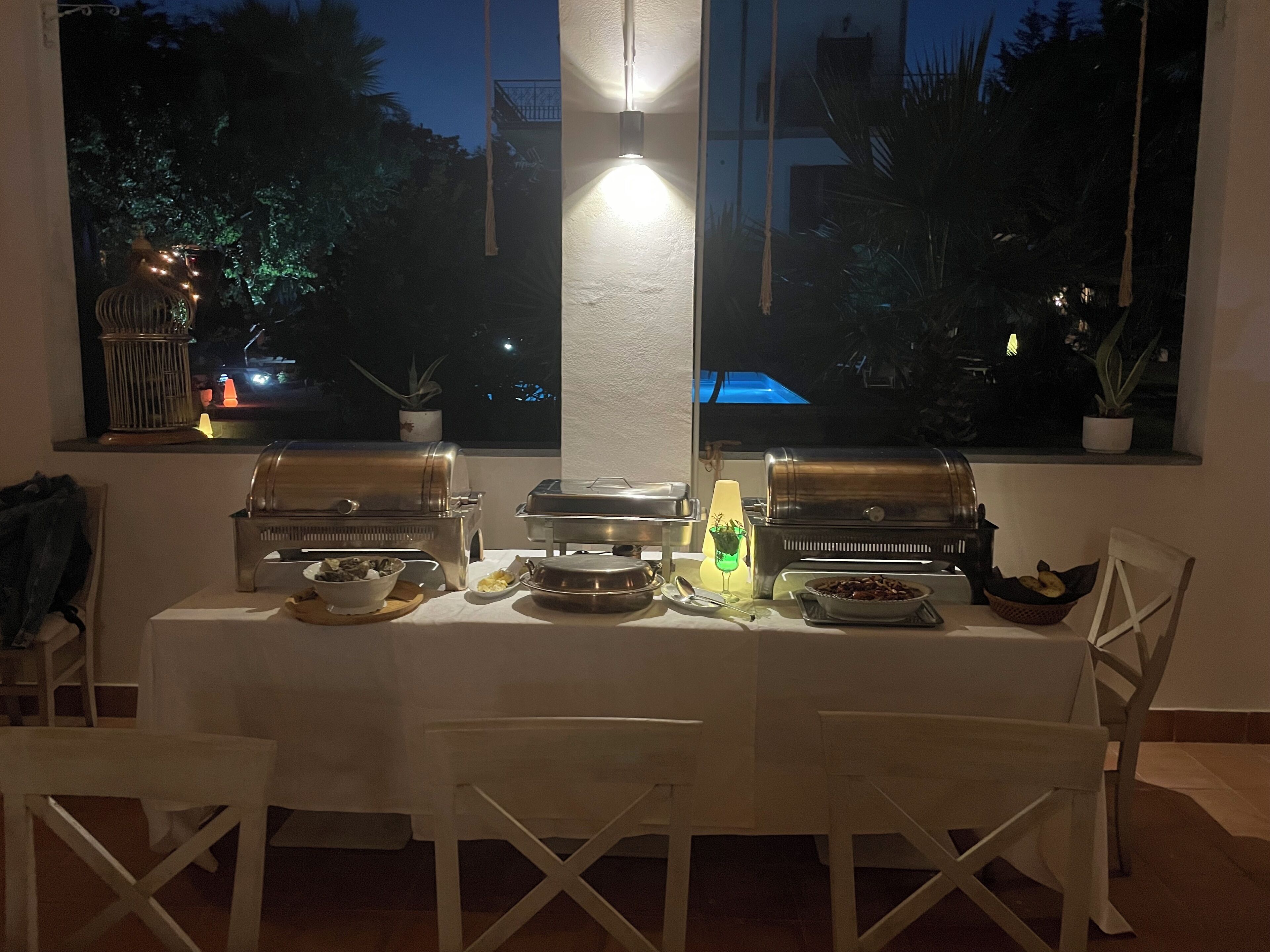Uma mesa de jantar posta para uma refeição, com uma churrasqueira, tigelas, pratos e uma vela.
