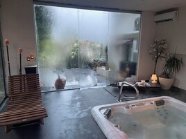 Casa de banho moderna com chuveiro de vidro, um banco de madeira, hidromassagem e uma planta em vaso.