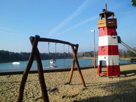 Uma praia com baloiço e um farol vermelho e branco ao fundo.