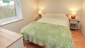 Quarto com uma cama, duas mesas de cabeceira com abajures, uma janela e um aviso de saída de incêndio, além de piso de madeira.