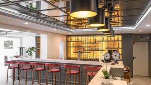 Uma área de bar moderna com um balcão comprido, banquetas vermelhas e uma seleção de garrafas de bebidas.