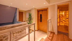 Um hall de hotel com parede de pedra, porta de madeira e escada com corrimão de metal.