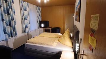 Quarto compacto com cama, escrivaninha, cadeira e televisão.