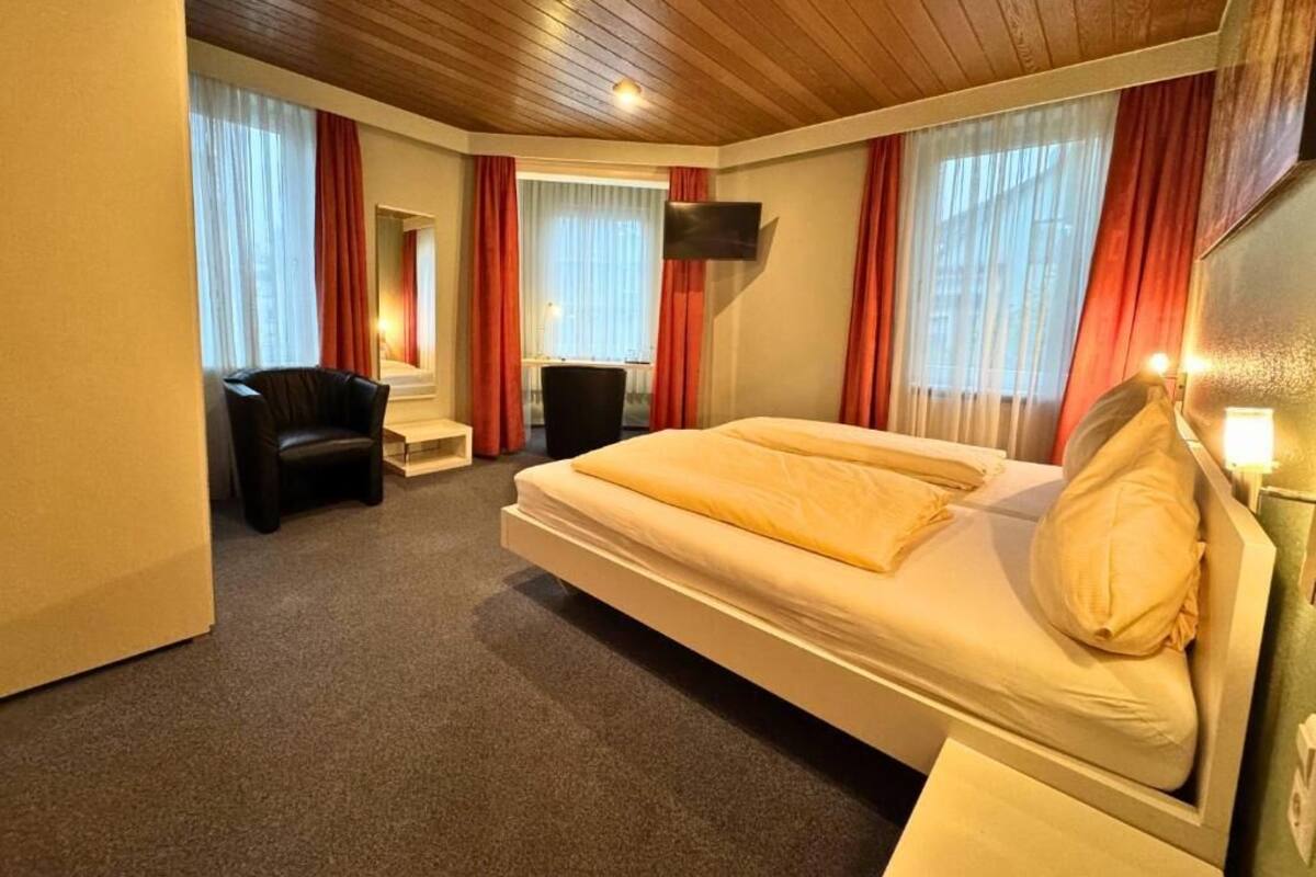 Quarto de hotel com cama, uma cadeira, escrivaninha e televisão.