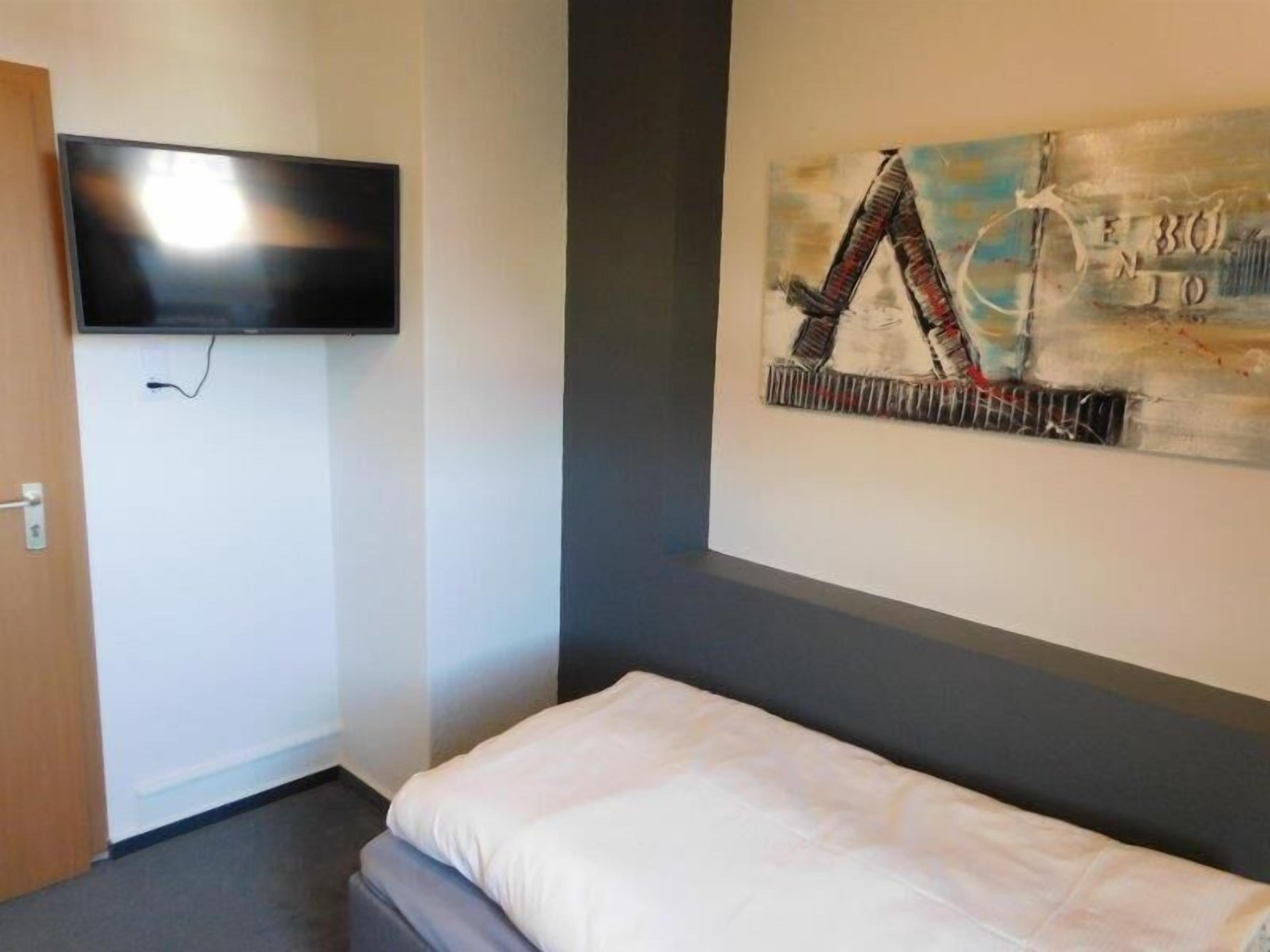 Quarto de hotel com uma cama, uma televisão de tela plana na parede e uma obra de arte abstrata acima da cama.