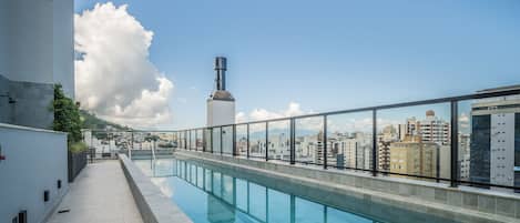 Uma piscina no terraço com vista para a cidade, um guarda-corpo de vidro e uma chaminé alta.