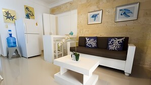 Uma sala de estar moderna com um sofá branco, uma mesa de centro e uma área de cozinha com um frigorífico e dispensador de água.