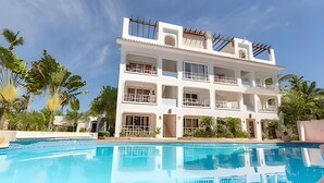 Um edifício com vários andares, varandas, piscina e vegetação tropical.