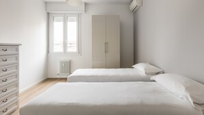 Quarto minimalista com um guarda-roupa espaçoso, cômoda e cama com roupa de cama branca.