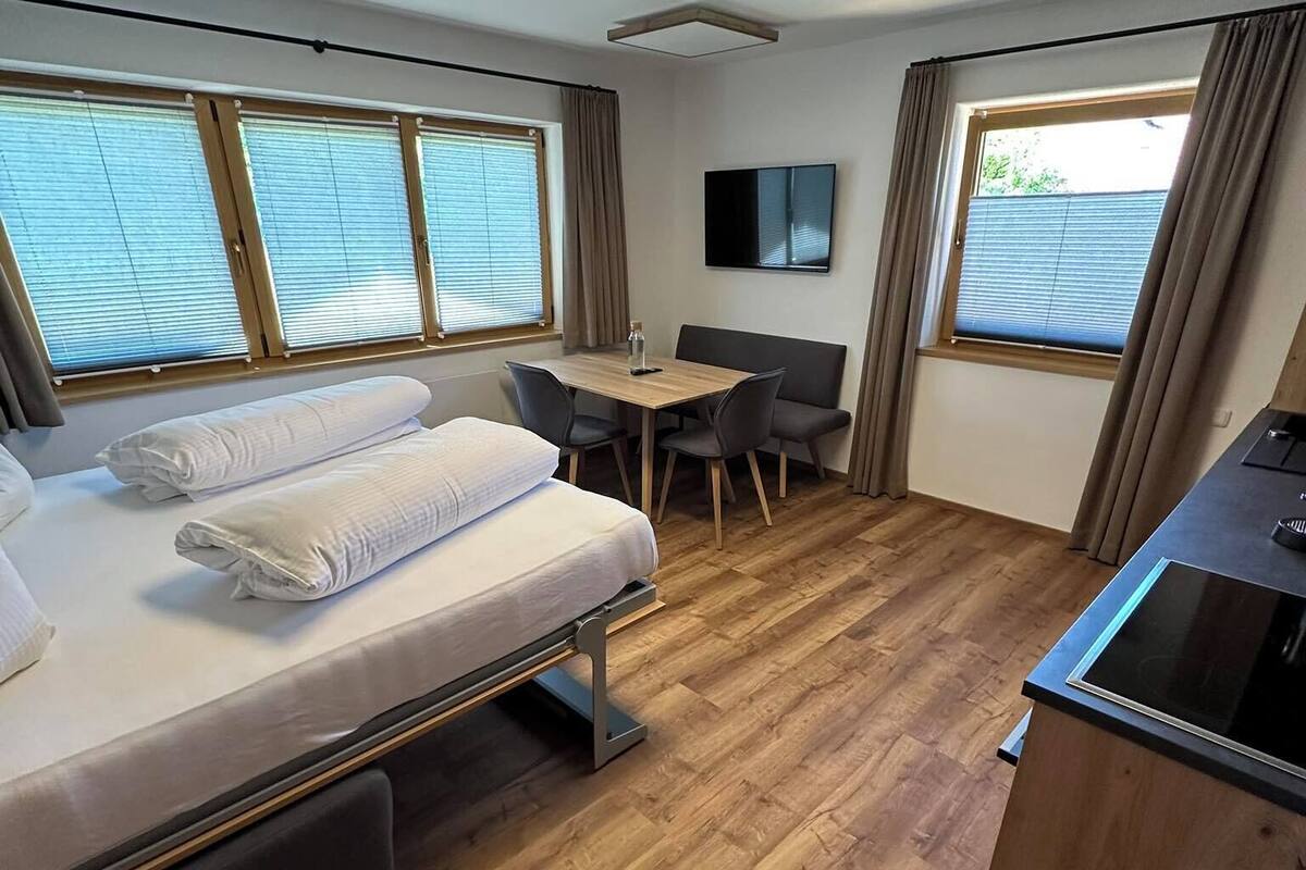 Quarto de hotel pequeno, com cama, uma mesa de refeições e uma cozinha compacta.