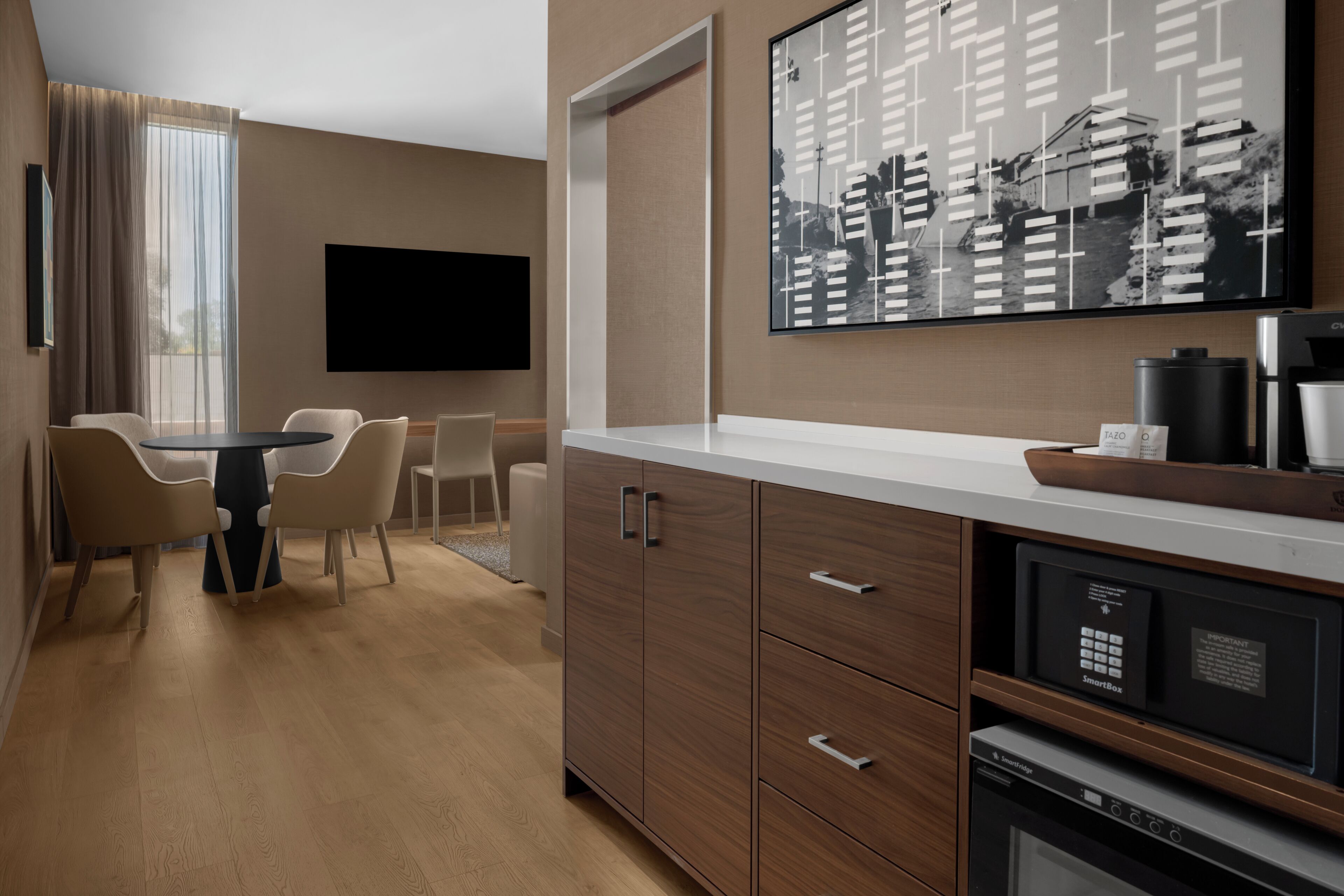 Quarto de hotel moderno com área de jantar, televisão de tela plana, máquina de café e forno embutido.