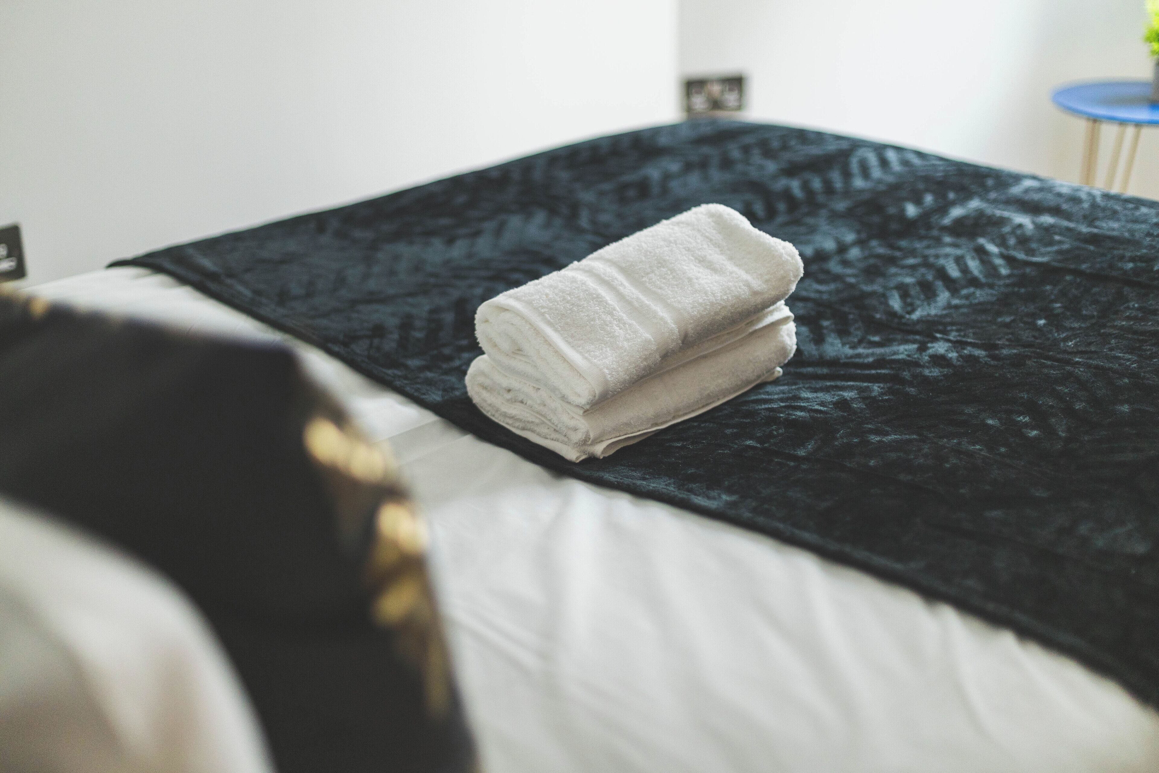 Cama bem arrumada com uma toalha branca dobrada por cima, um cobertor preto texturizado e um travesseiro branco.