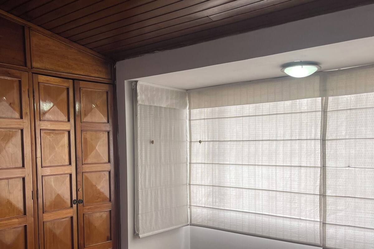 Quarto com armário de madeira, colcha roxa e janela com cortinas finas.