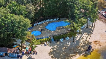 Vista aérea de um resort com várias piscinas, cadeiras de descanso e uma área de praia.