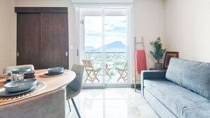 Uma área de refeições com uma mesa posta para quatro pessoas, um sofá e uma porta de vidro deslizante que dá para uma varanda com vista para as montanhas.