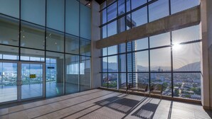 Interior espaçoso com grandes janelas que oferecem vista da cidade, piso em mosaico e uma placa visível na porta de vidro.