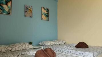 Quarto com duas camas, cada uma com roupa de cama estampada com flores e almofadas castanhas. Três quadros pendurados na parede, e o quarto tem uma paleta de cores azul claro e bege.