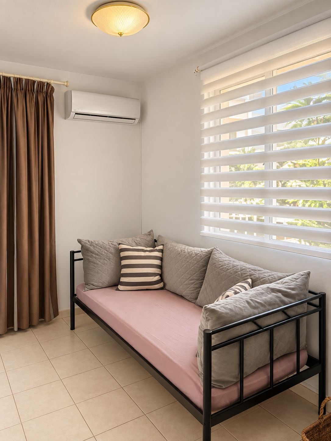 Uma cama de solteiro com cabeceira, uma janela com persianas, um aparelho de ar condicionado e uma cortina.
