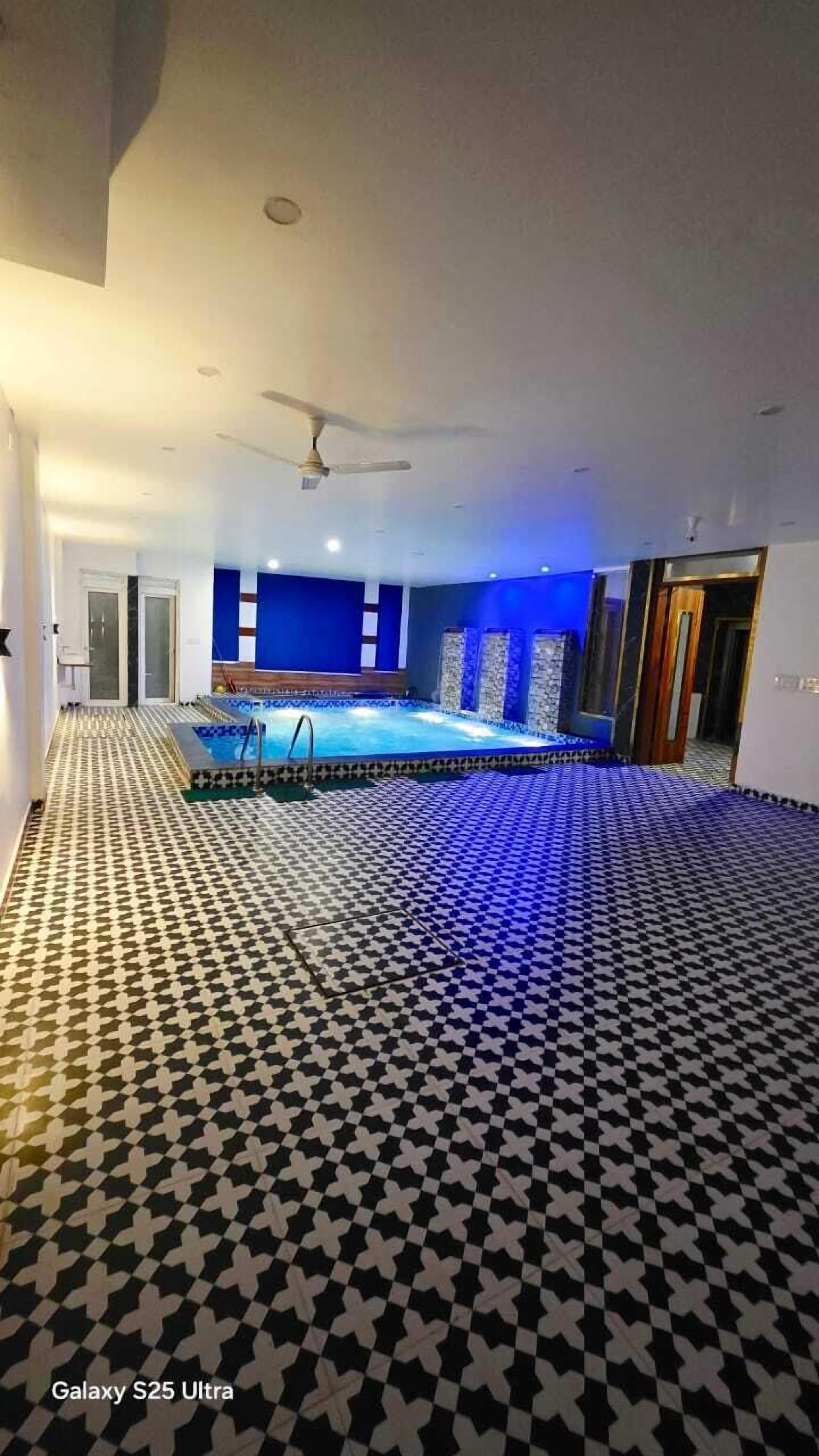 Um quarto amplo com piso estampado, área de piscina com iluminação azul e ventilador de teto.
