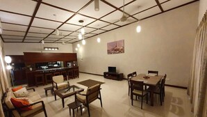 Uma sala de estar ampla, com uma mesa de jantar, sofás e uma cozinha ao fundo.