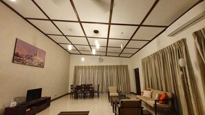 Uma sala de estar ampla com teto alto, televisão de tela plana, mesa de jantar, sofás e cortinas.