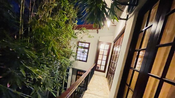 Um corredor estreito com chão de azulejos, grades de madeira e vista para um edifício tradicional com grandes janelas e uma porta com padrão de grade.