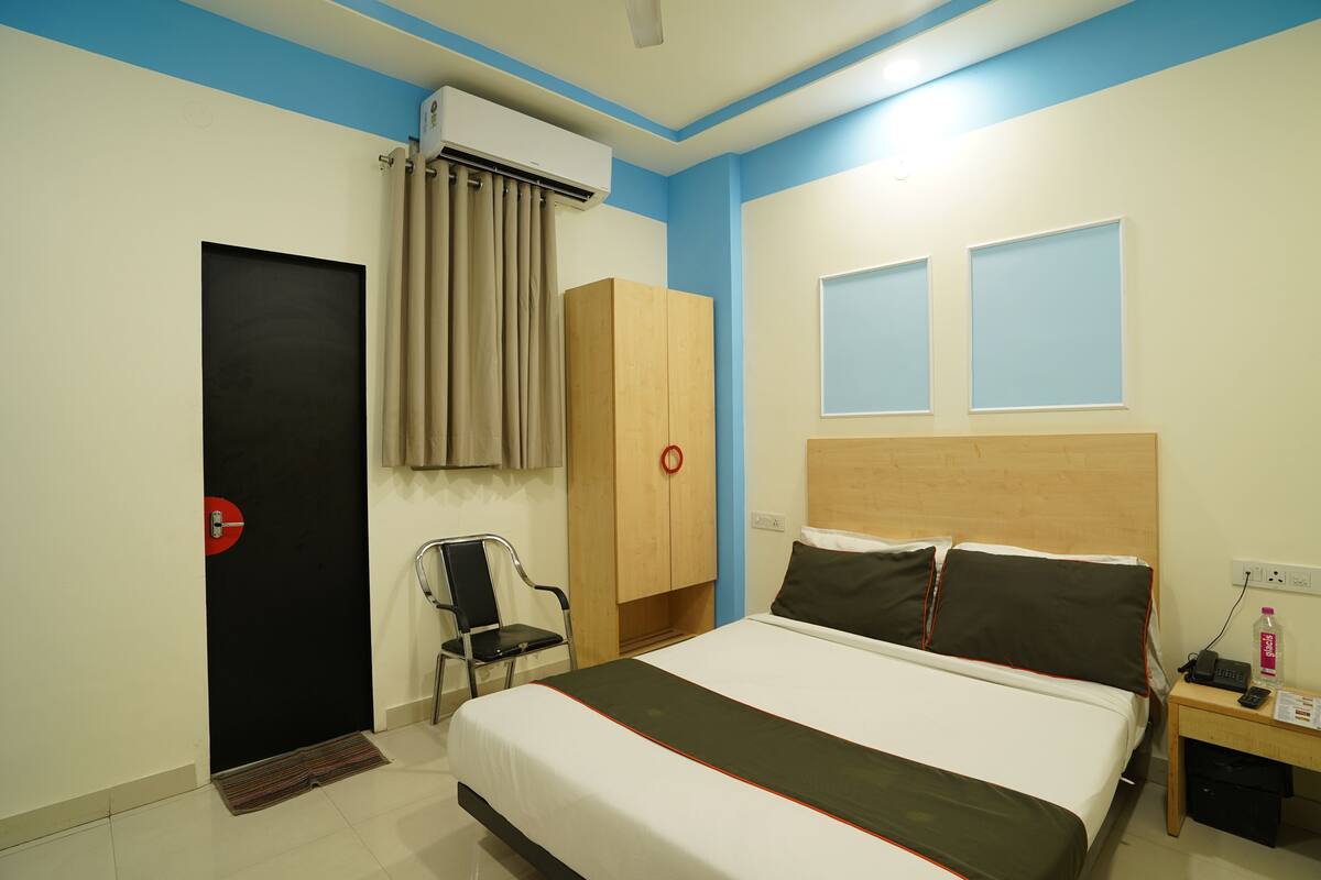 Quarto de hotel com cama, escrivaninha, cadeira, guarda-roupa e ar condicionado.